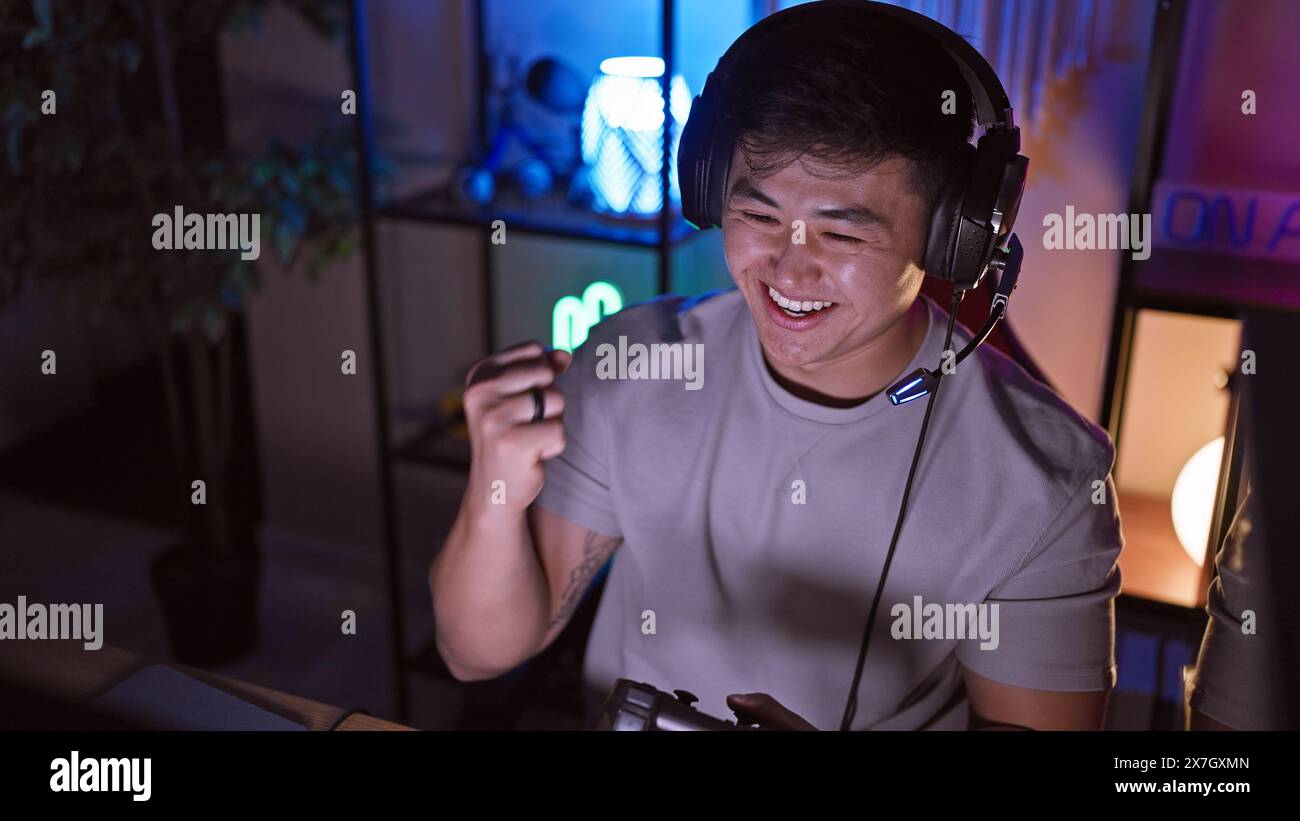 A happy asian man gaming in a dark room with led lights wearing ...