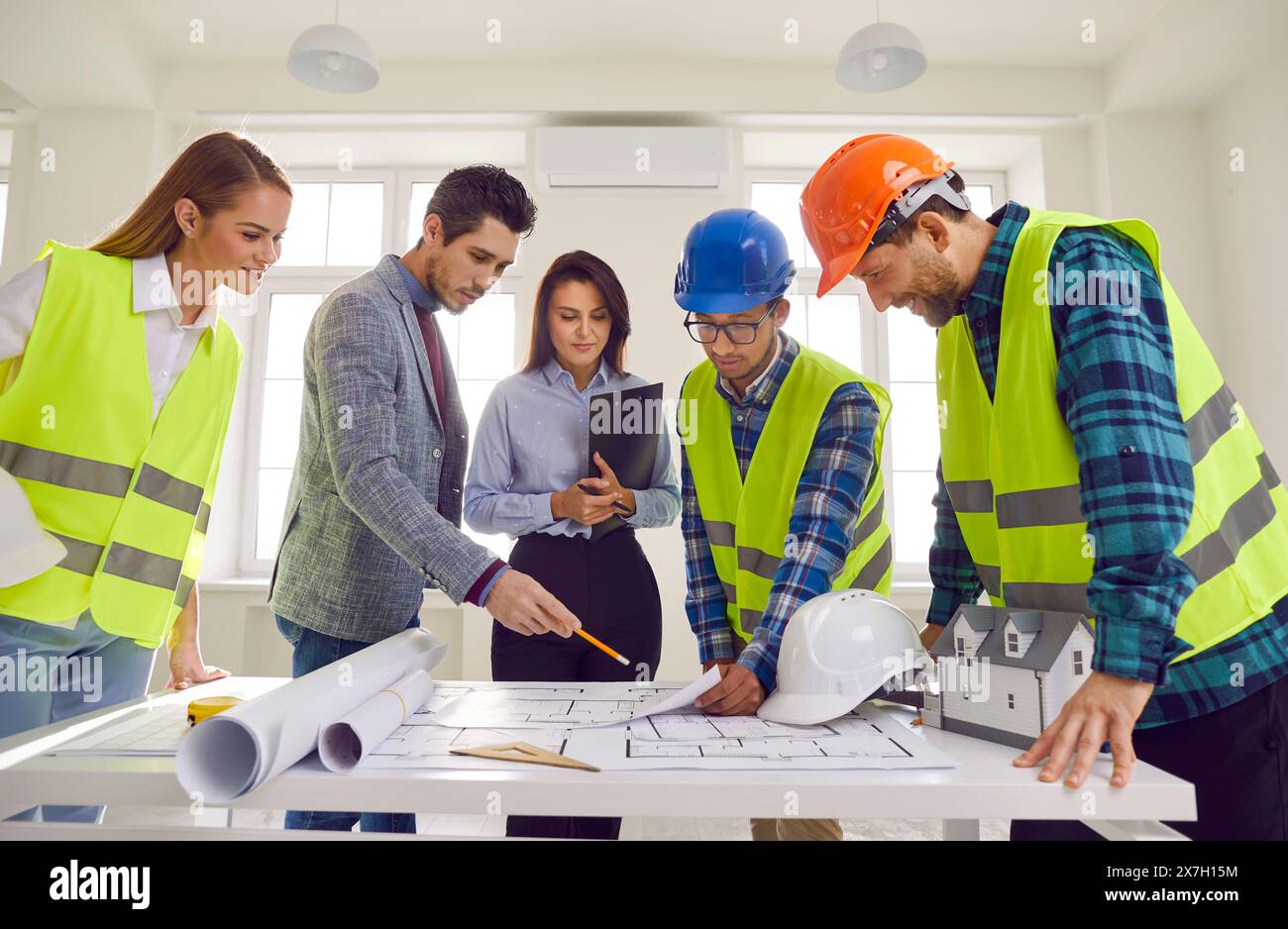 Construction team standing around office table and looking at paper ...