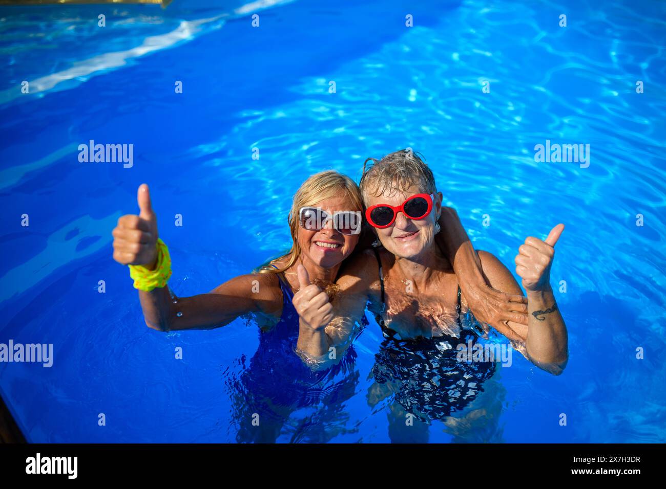 Group of cheerful seniors shaving fun in pool jumping, swiming and ...