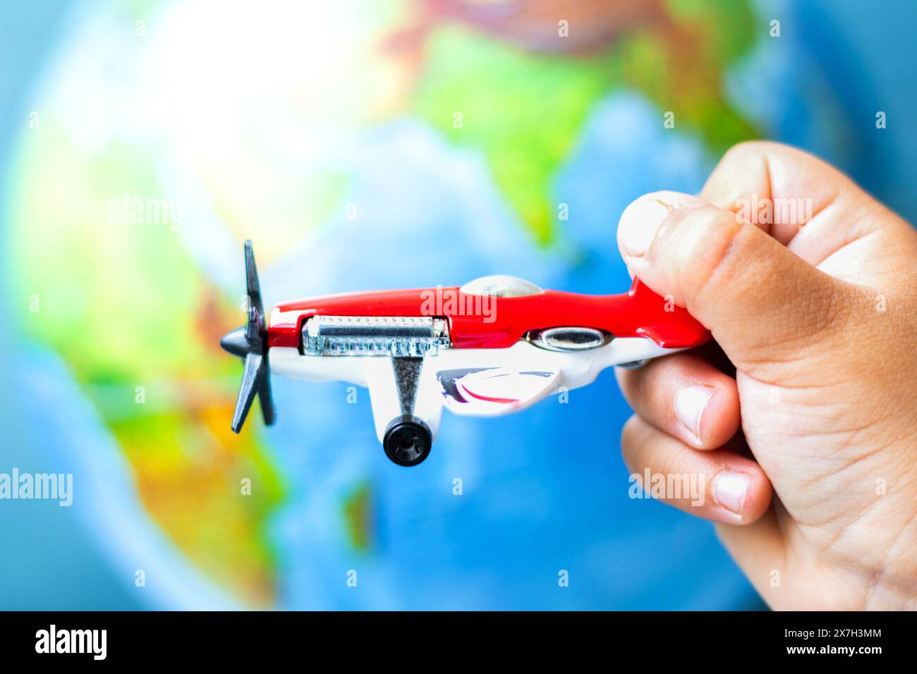 Child hand holding toy propeller plane in front of earth background ...