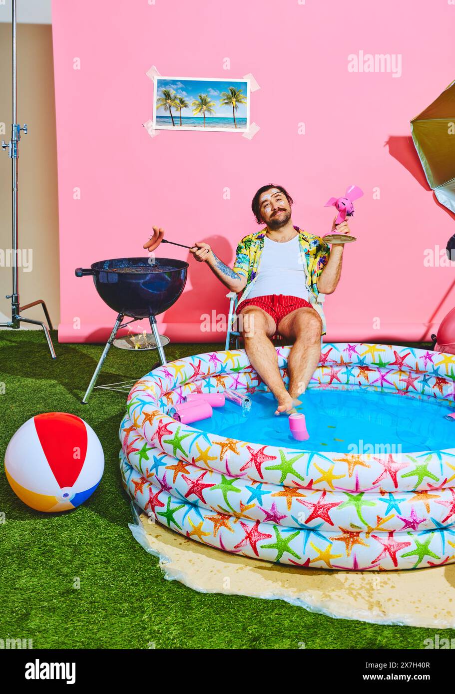 Young man in vibrant outfit with Hawaiian shirt relaxing in inflatable swimming pool and cooking ...