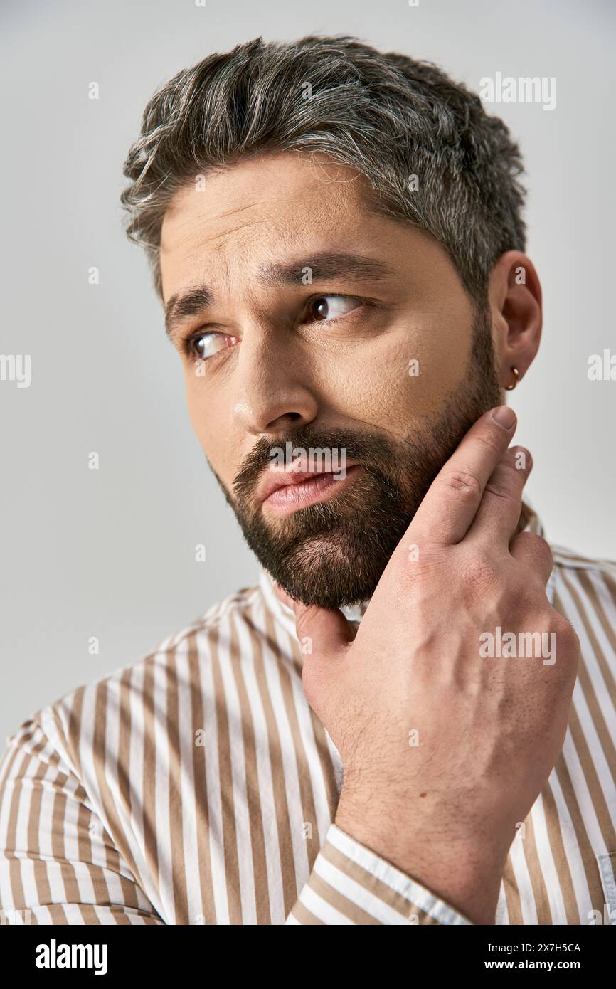 A captivating man with a beard poses in elegant attire against a grey ...