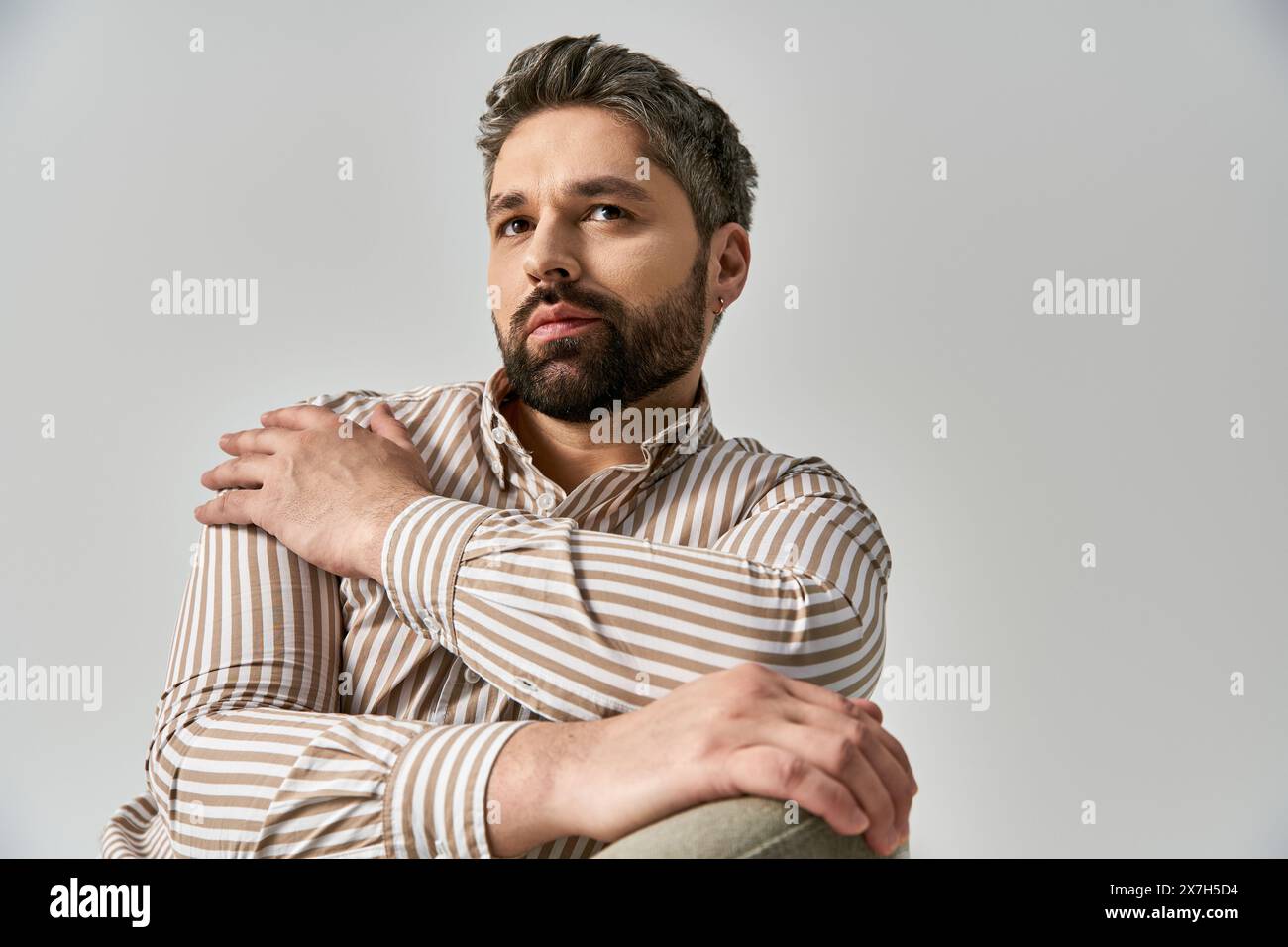 A stylish man with a beard striking a pose in a striped shirt against a ...
