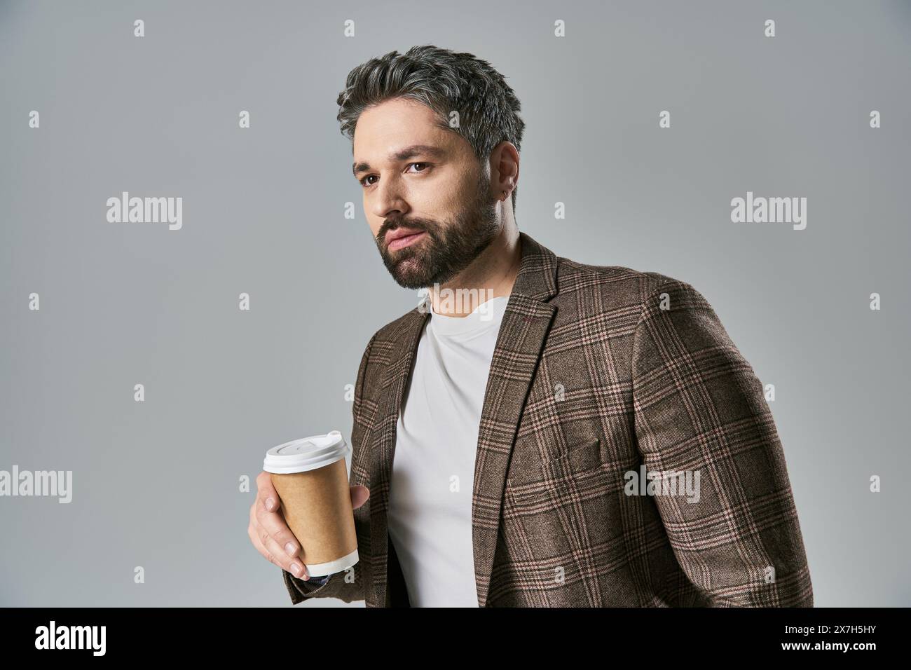A stylish man with a beard elegantly holds a cup of coffee, exuding ...