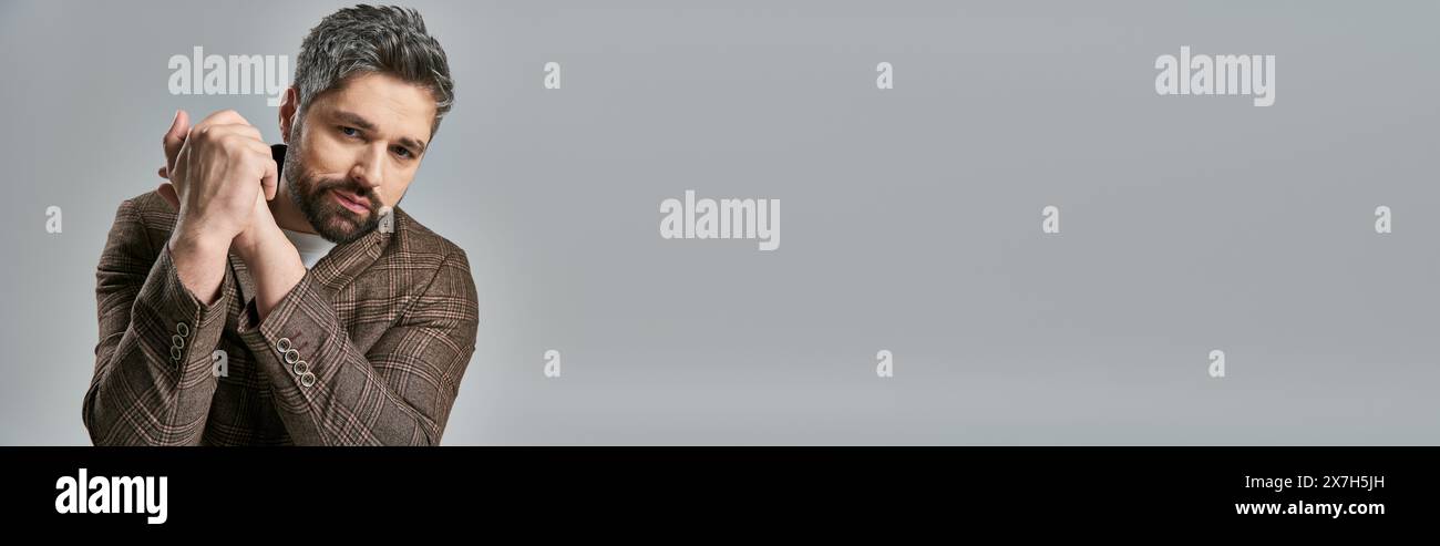 Stylish man with beard in elegant brown suit posing on a grey studio ...