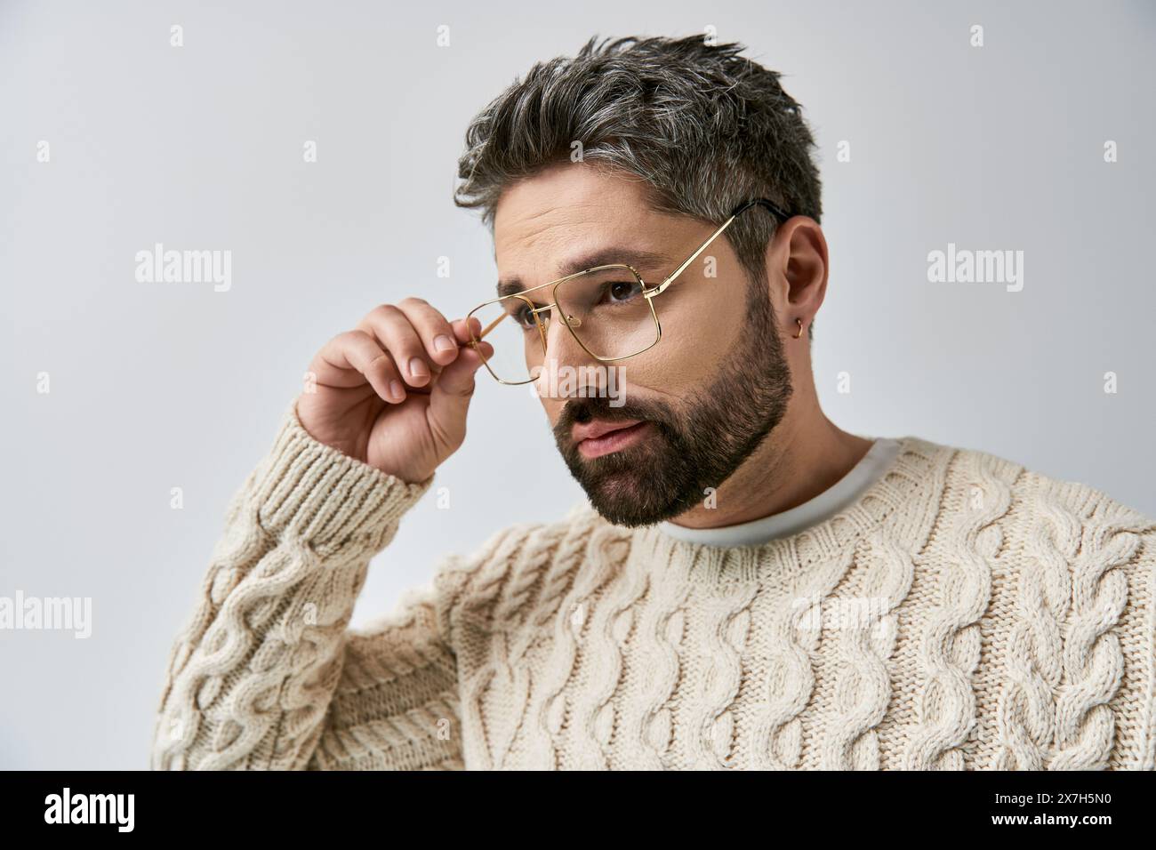A charismatic man with a beard poses in a white sweater against a grey ...