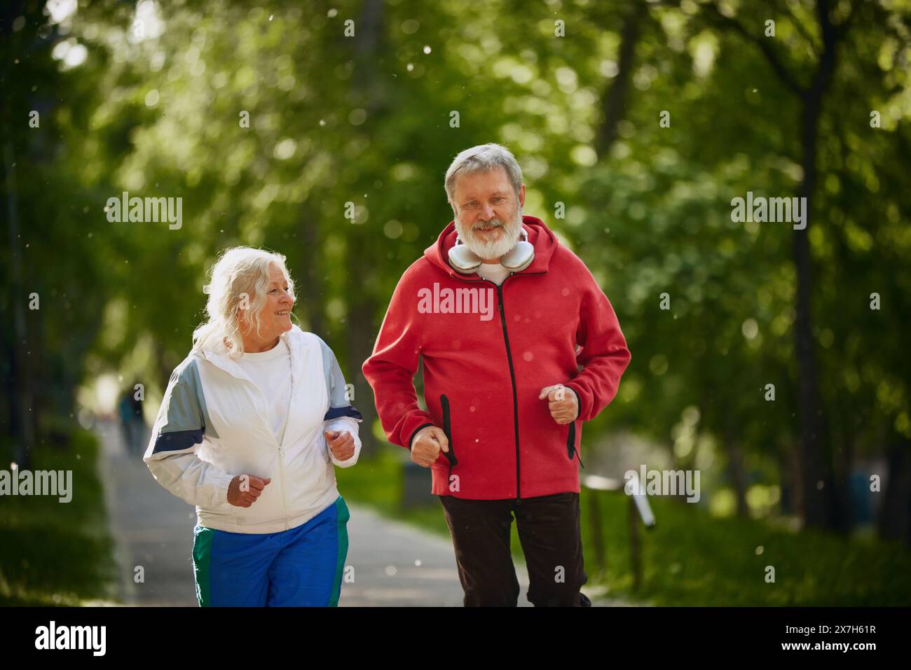 Elderly couple, jogging together in serene park on early summer morning, man and woman doing ...