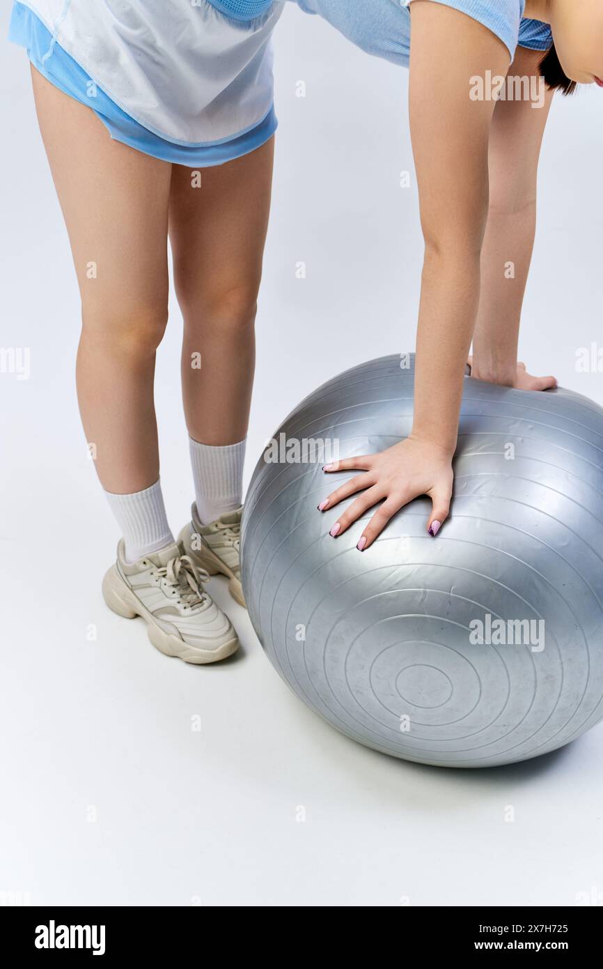 A pretty, brunette teenage girl in sportive attire gracefully balances on an exercise ball ...