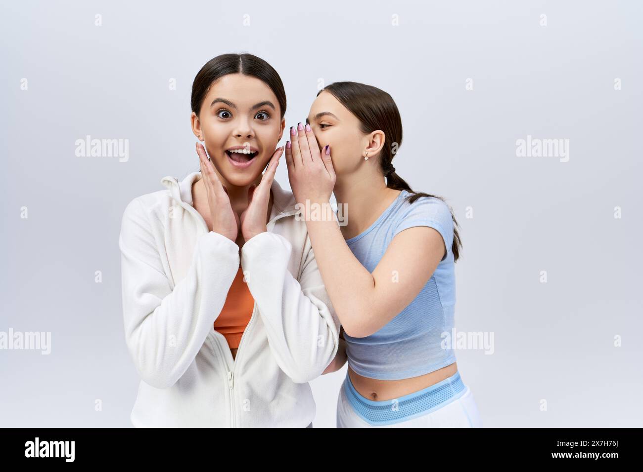 Two pretty, brunette teenage girls in sportive attire standing side by ...