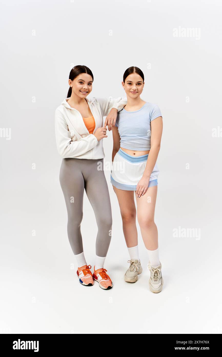 Two pretty, brunette teenage girls in sportive attire stand side by ...