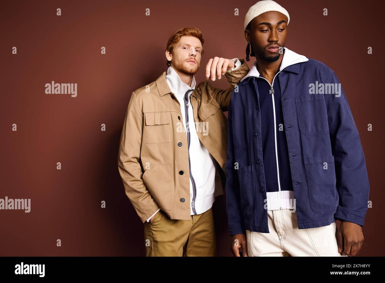 Two stylish multicultural men standing together in front of a brown ...