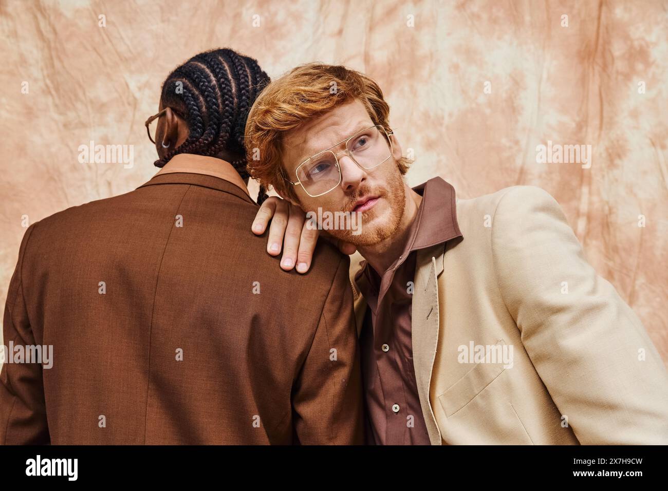 Two multicultural men dressed in dapper style hug in front of a wall ...
