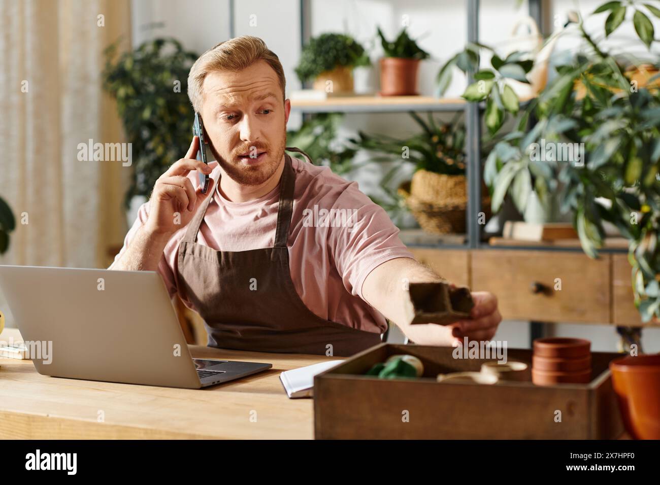 A man sits at a table in a plant shop, engaged in a phone call while ...