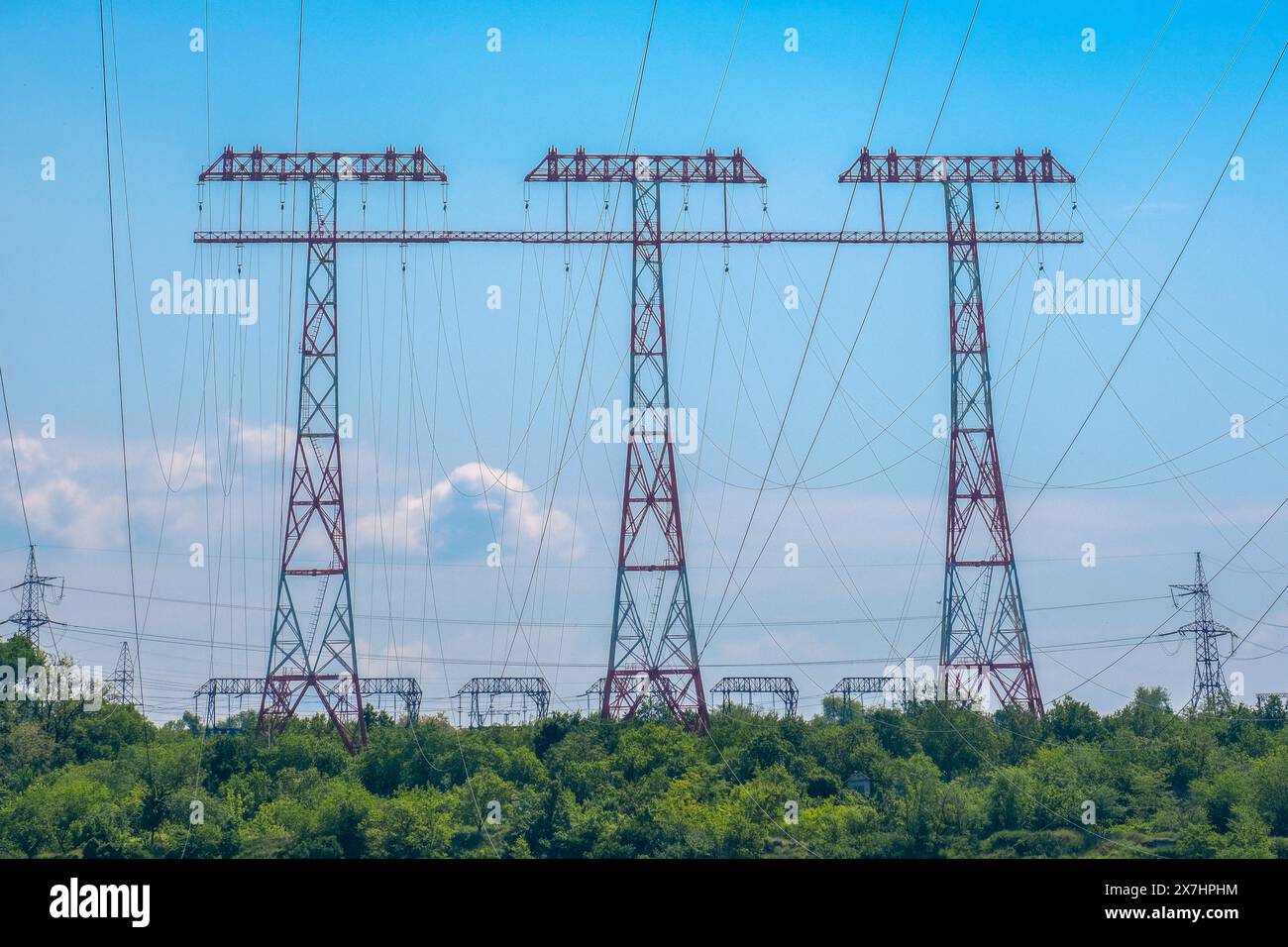 High voltage power lines tower over a lush green landscape against a ...