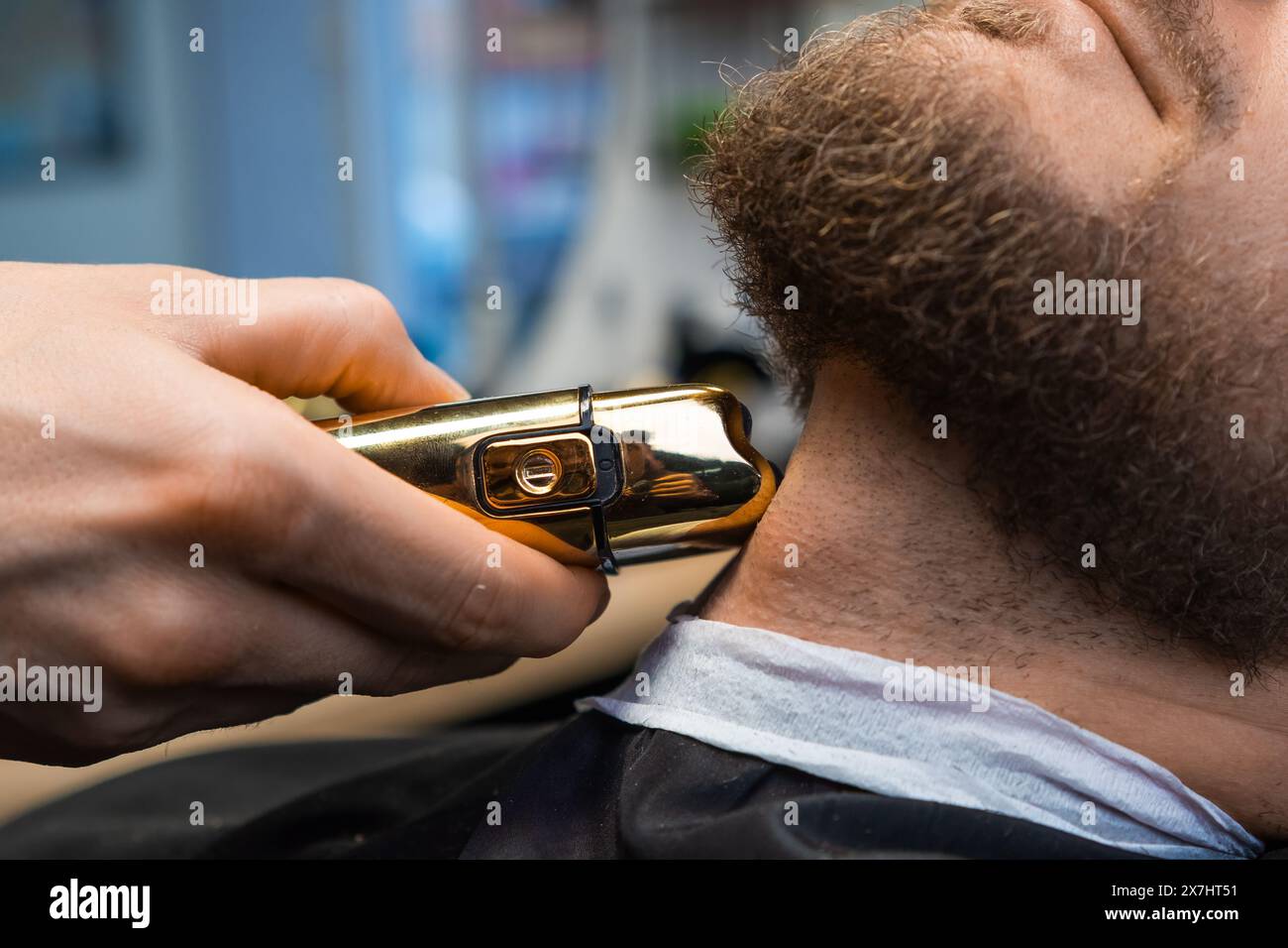 Master barber employs an automatic trimmer to groom the clients beard ...