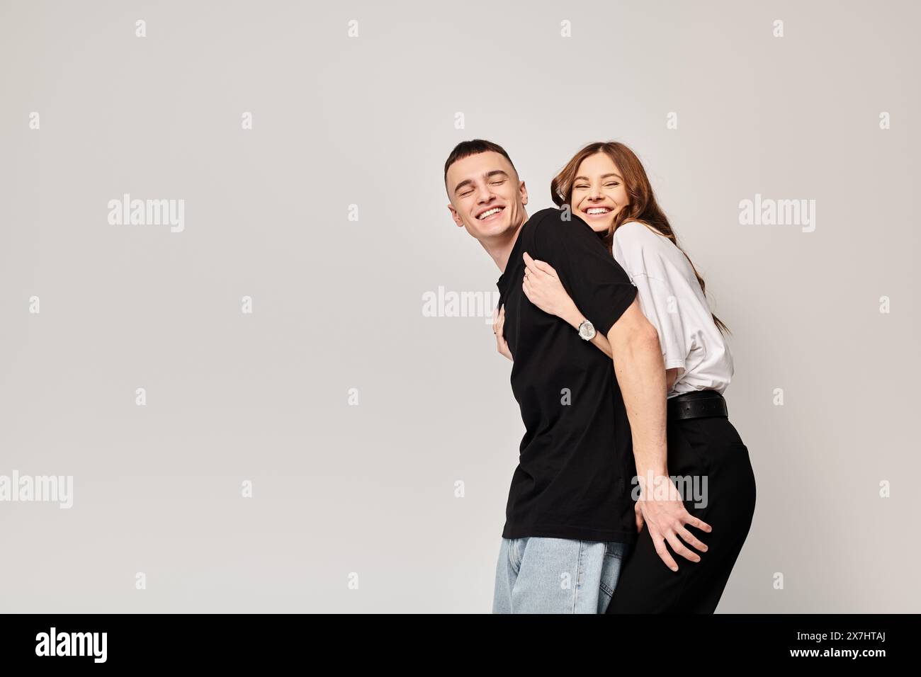 A man and woman, young couple, hugging each other affectionately in a studio with a grey ...