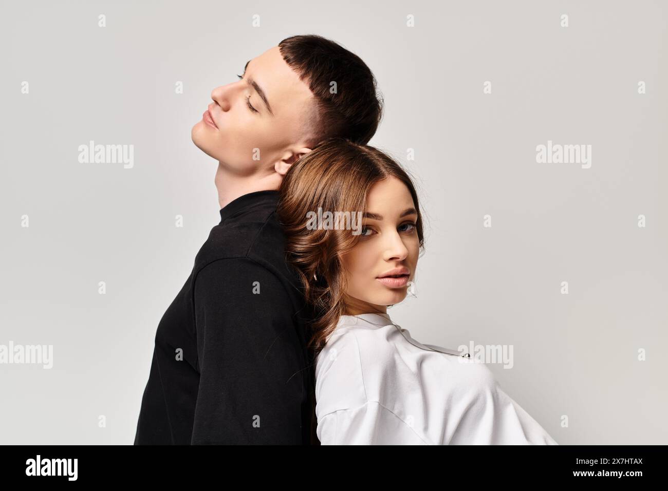 A young couple standing side by side in a studio with a grey background ...