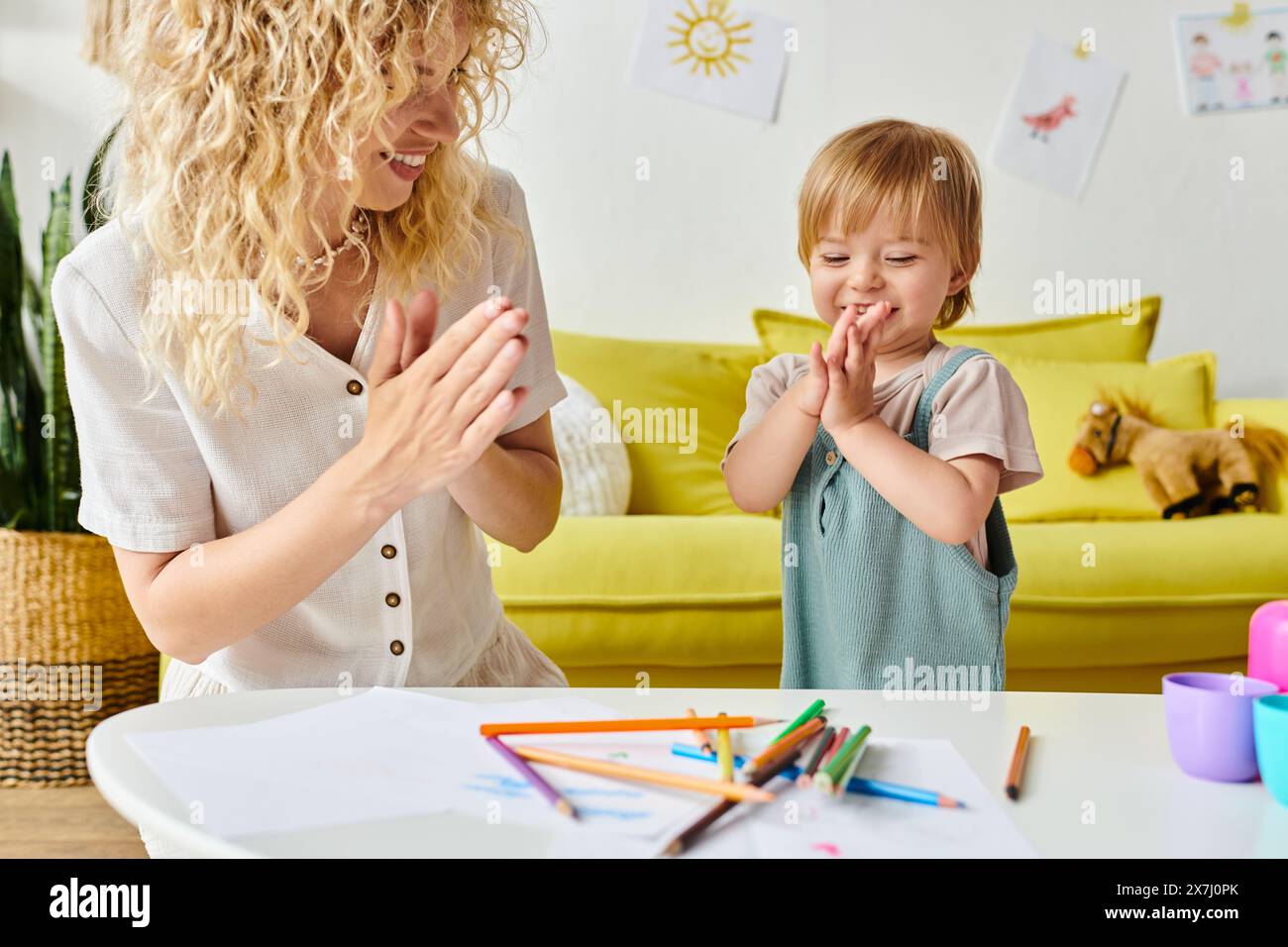 A curly mother stands next to her toddler daughter, embracing ...