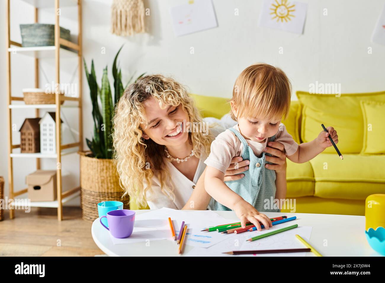 A curly-haired mother and her toddler daughter sit at a table ...
