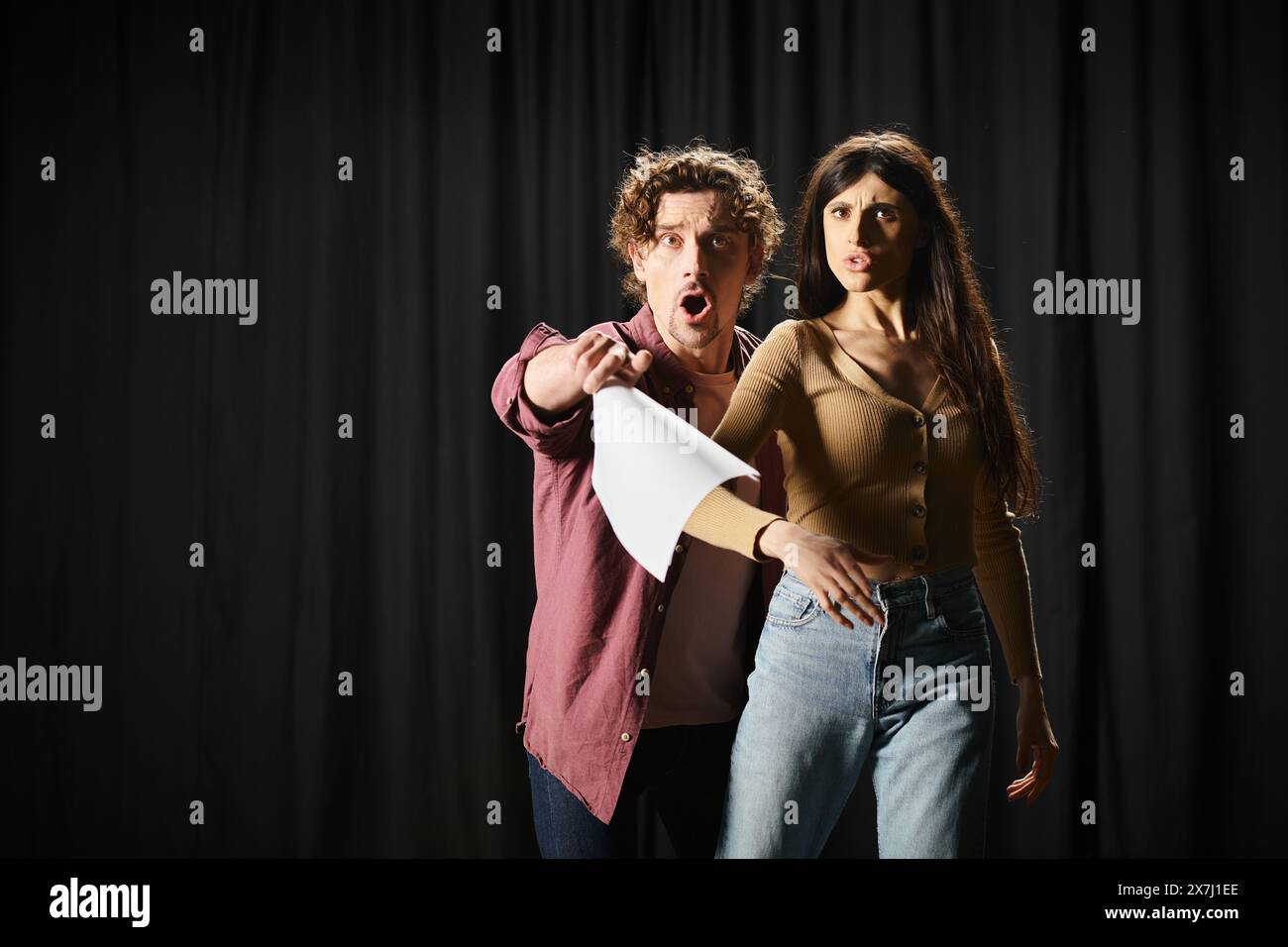 A stylish man and woman pose confidently in front of a black curtain ...