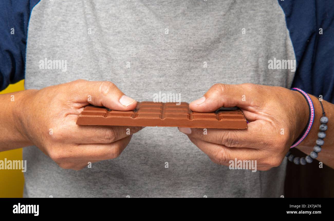 hands of an unrecognizable man breaking a chocolate bar to consume it ...