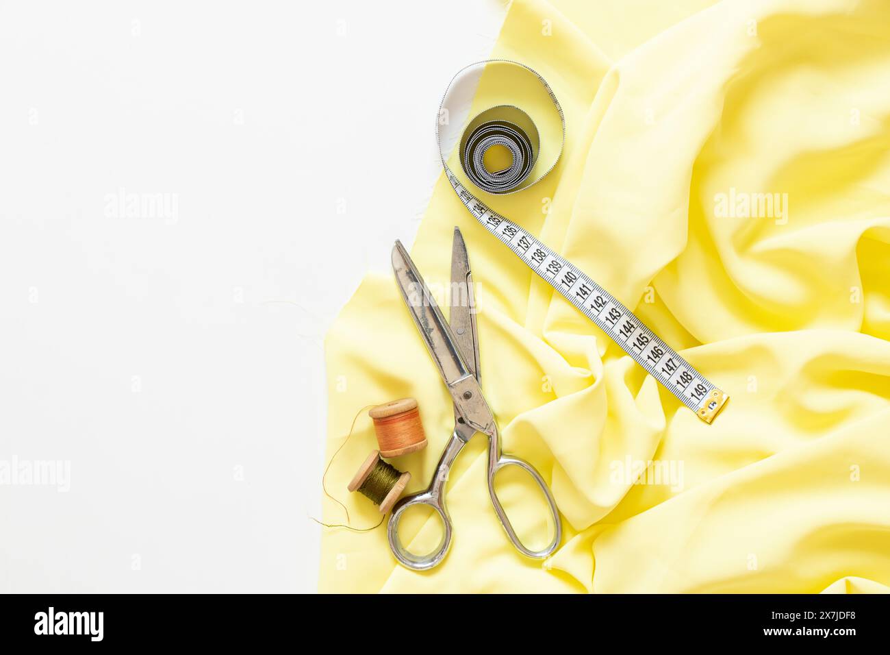 Spools of thread, measuring tape, sewing scissors and yellow fabric on ...