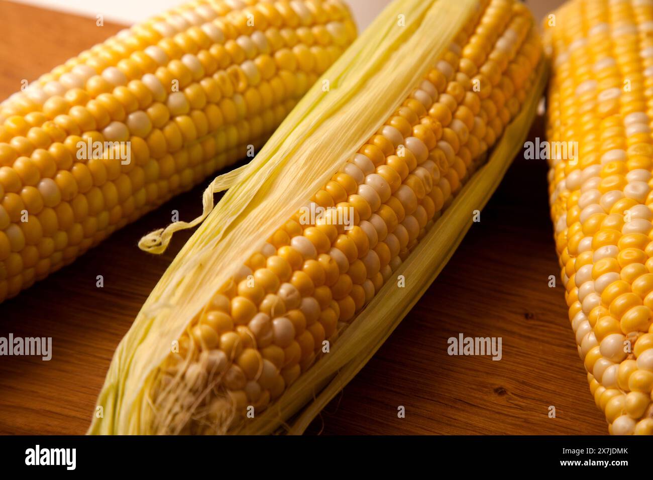 Clous up view of cutting board with three ears of ripe sweet corn on ...