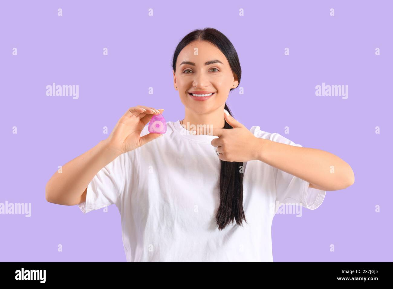 Beautiful young happy woman pointing at dental floss on purple ...