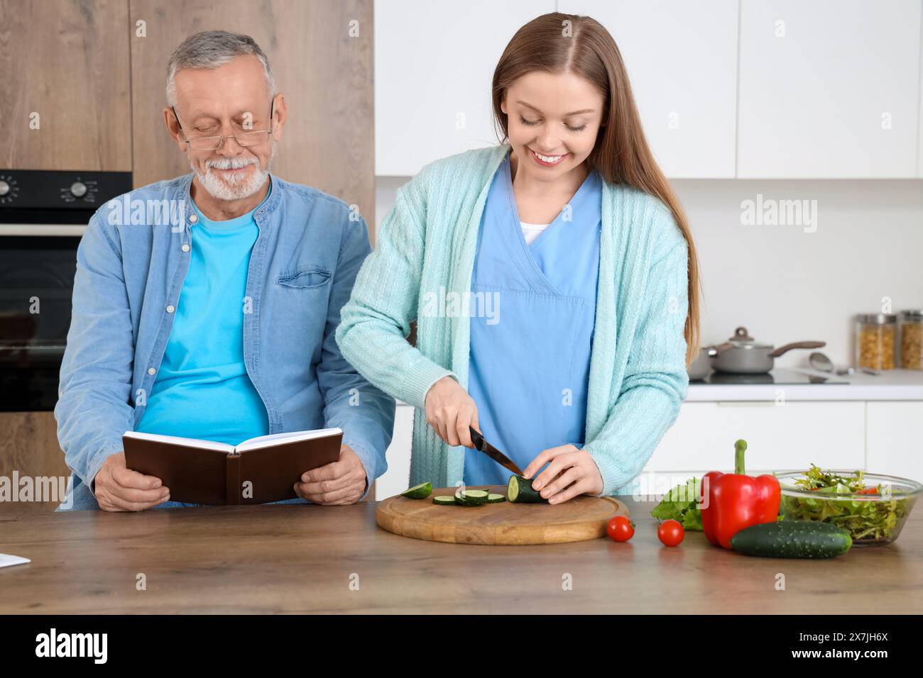 Senior man reading book with nurse cooking in kitchen Stock Photo - Alamy