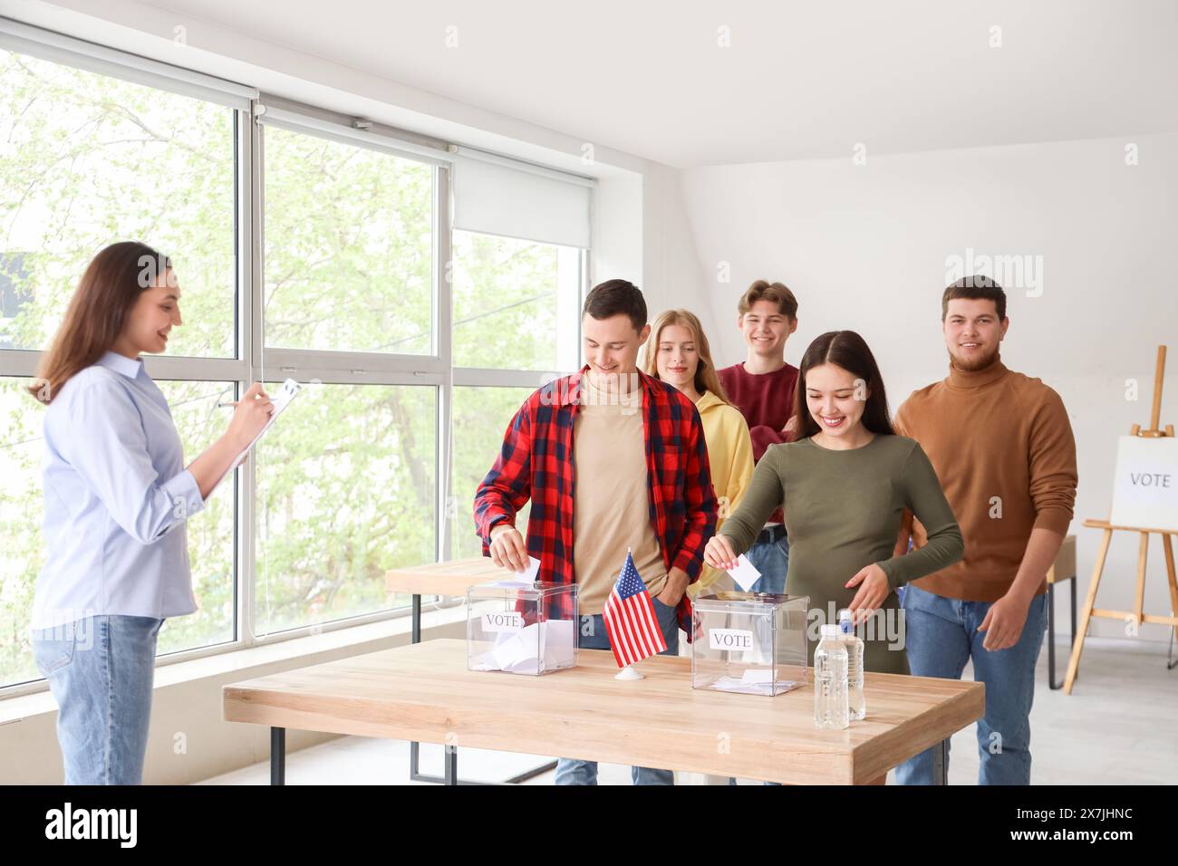 Voting young people with USA flag near ballot boxes at polling station ...
