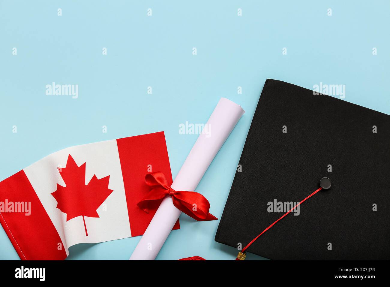 Diploma with red ribbon, Canadian flag and graduation hat on light blue ...