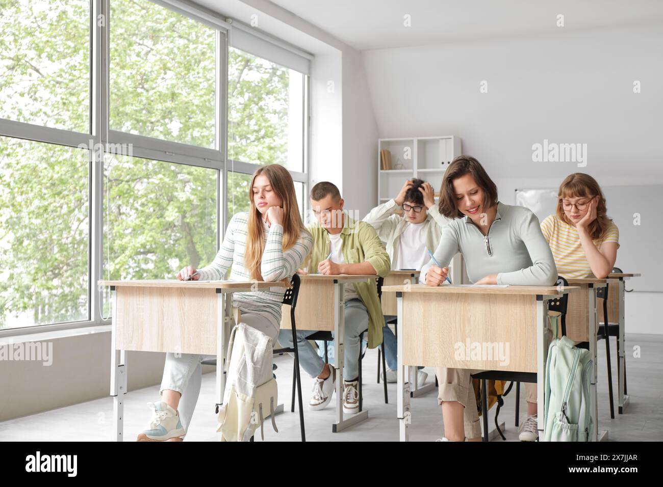 Students passing exam at desks in classroom Stock Photo - Alamy