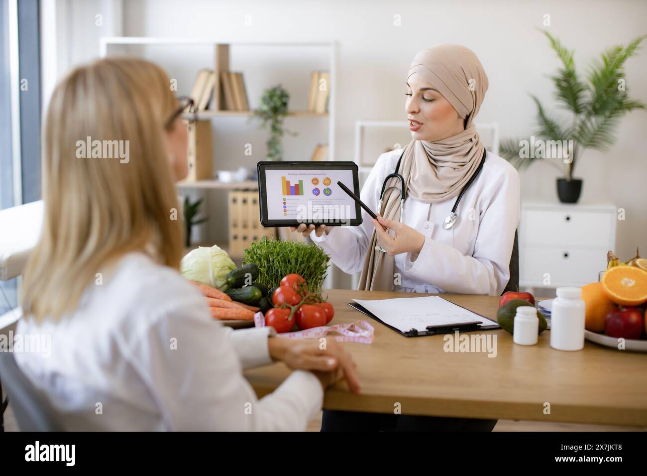 Muslim female doctor showing on tablet graphs of food for healthy ...
