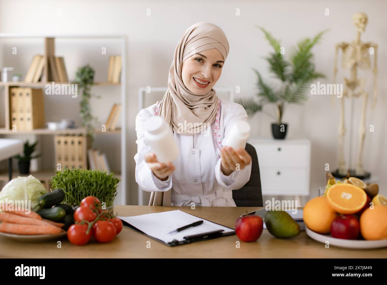 Portrait of positive Muslim lady in hijab and lab coat smiling at ...