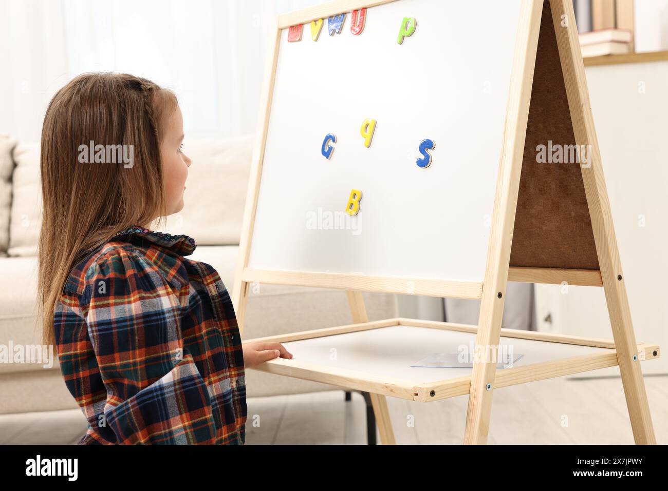 Cute little girl putting magnetic letters on board at home. Learning ...