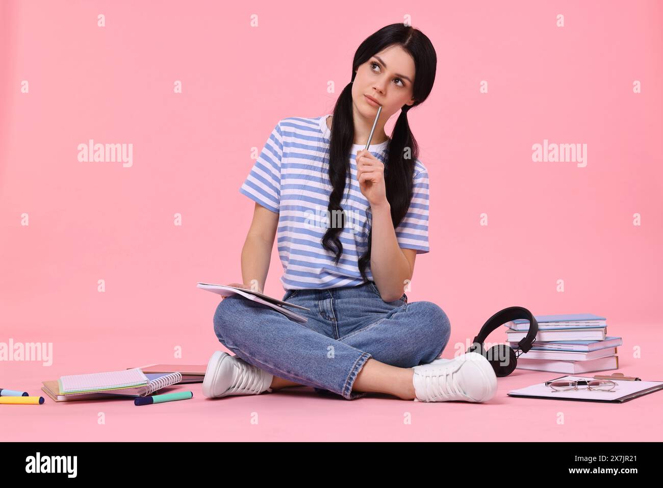 Student with notebook sitting among books and stationery on pink ...