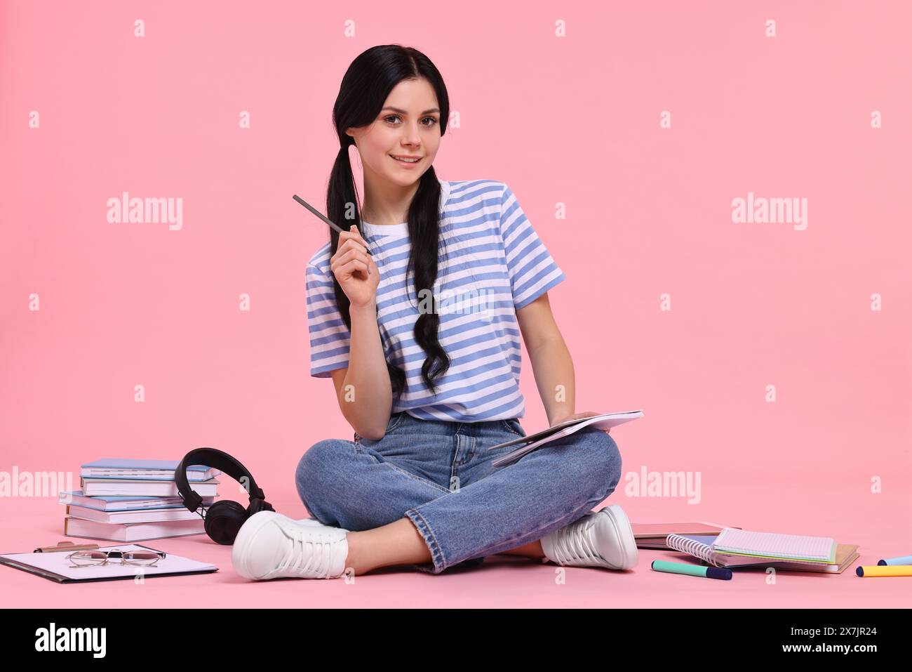 Smiling student with notebook sitting among books and stationery on ...