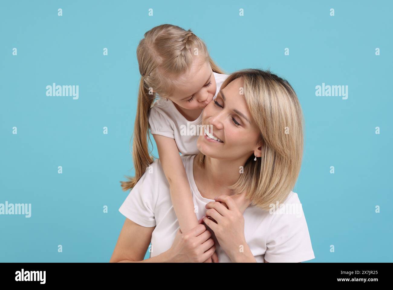 Daughter kissing her happy mother on light blue background Stock Photo ...