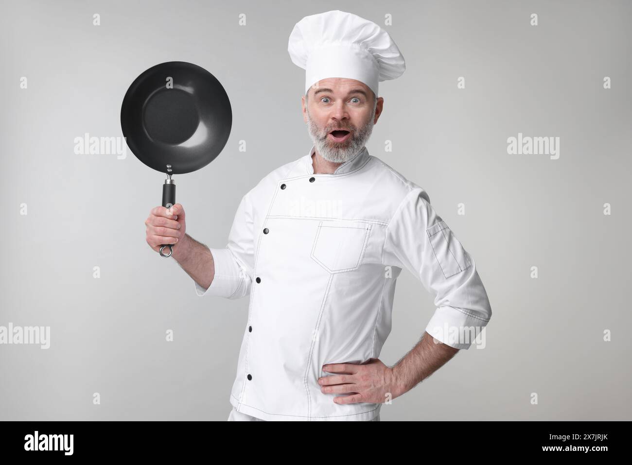 Surprised chef in uniform holding wok on grey background Stock Photo ...