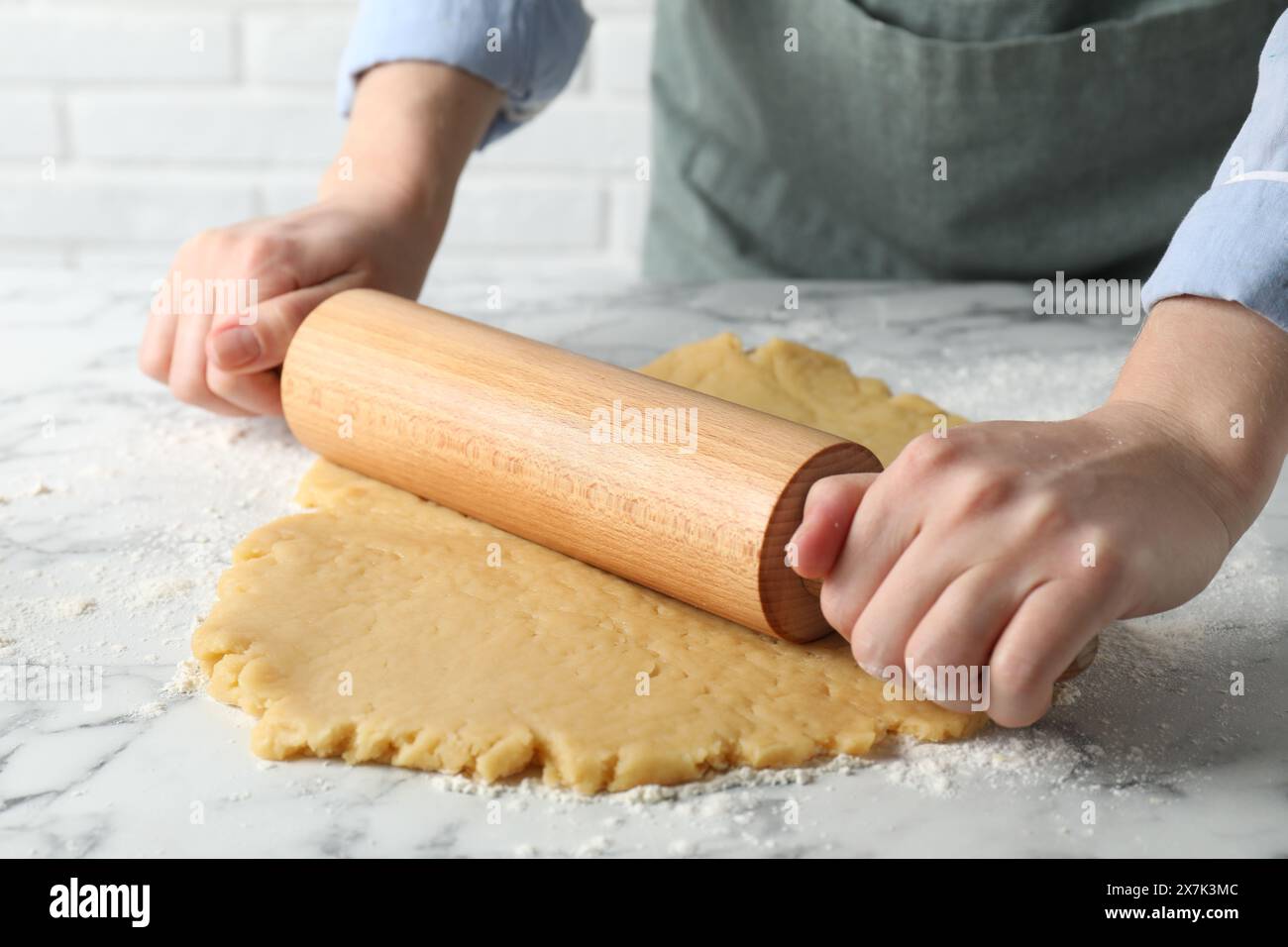 Making shortcrust pastry. Woman rolling raw dough at white marble table ...