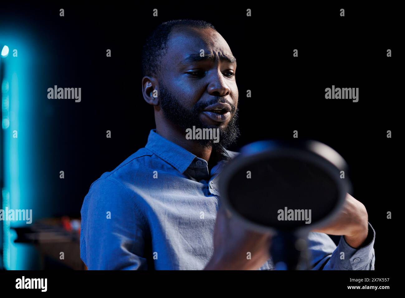Content creator in dark room using recording mic to shoot intro for ...