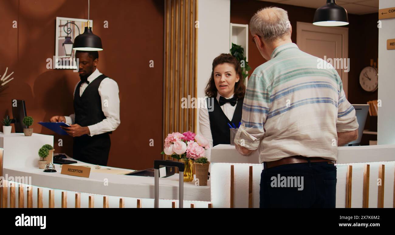 Elderly person arriving at hotel front desk with trolley bags, asking ...
