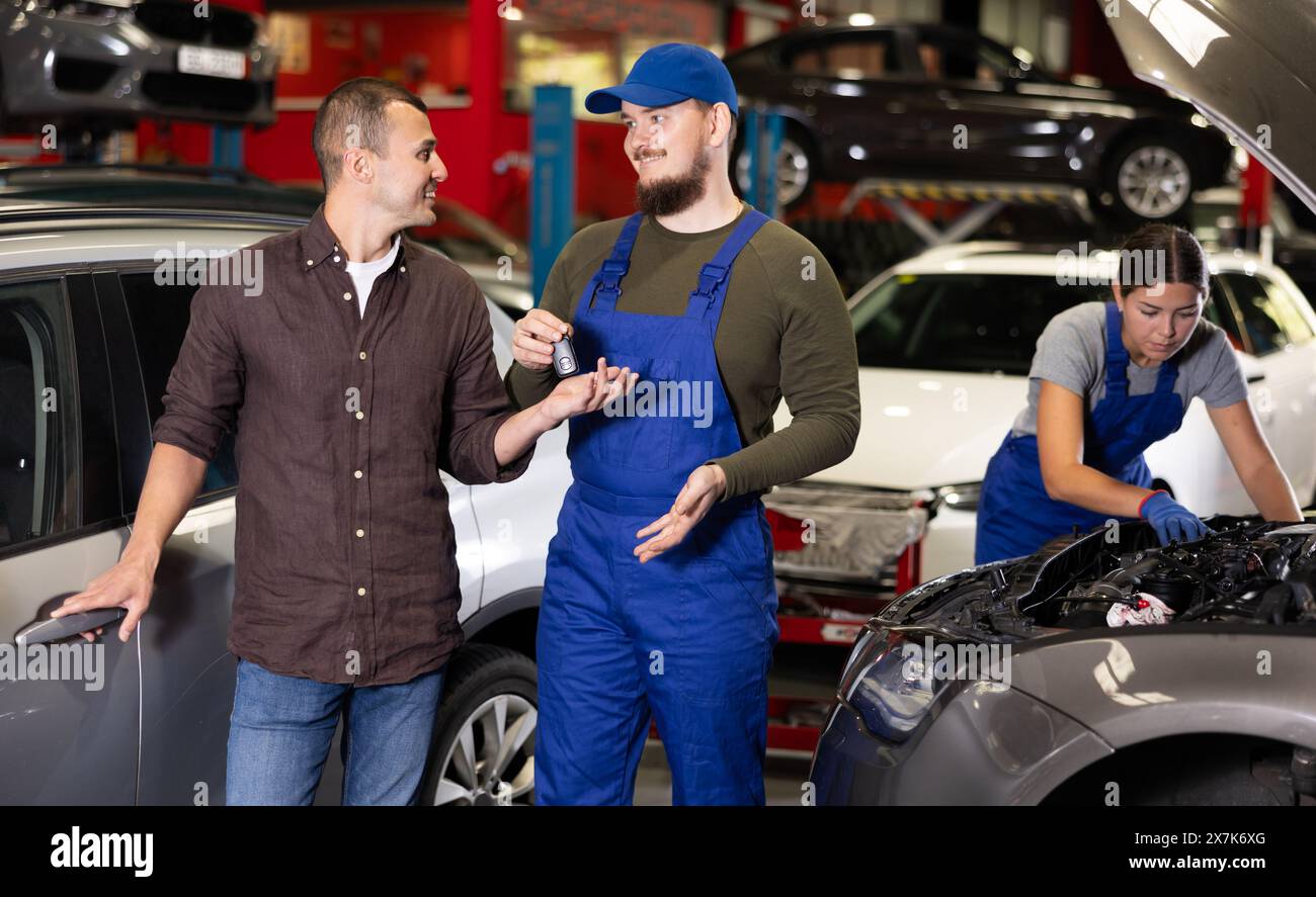 Happy man next to car being repaired. Auto mechanic gives man keys to ...