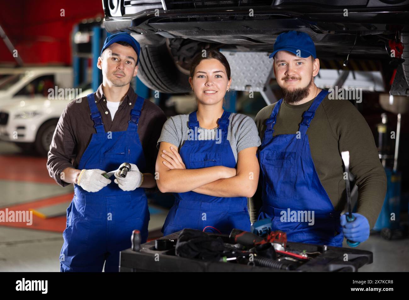 Two positive car mechanics and female worker inviting clients in auto ...