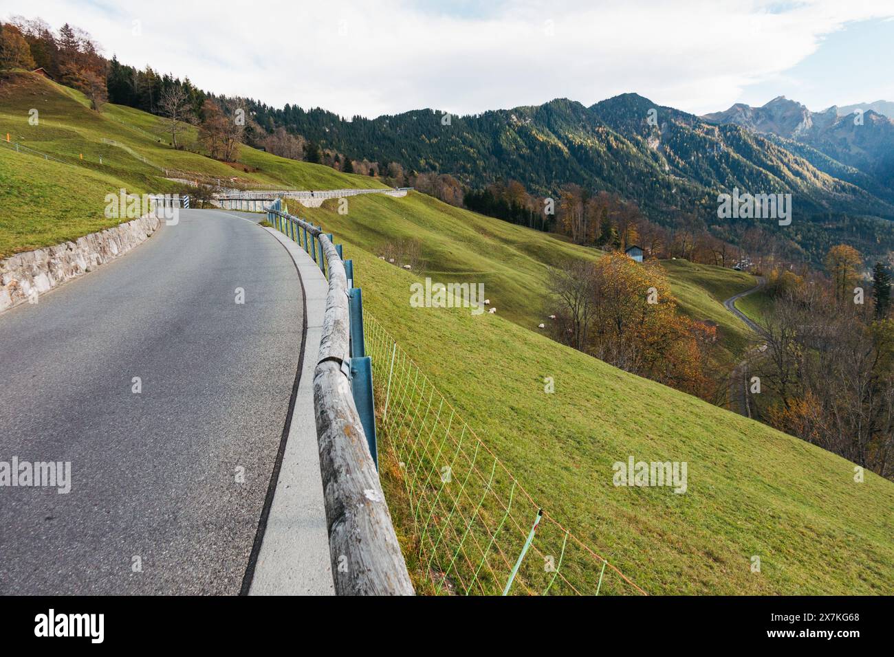 A winding road with a wooden safety barrier curves through rolling ...