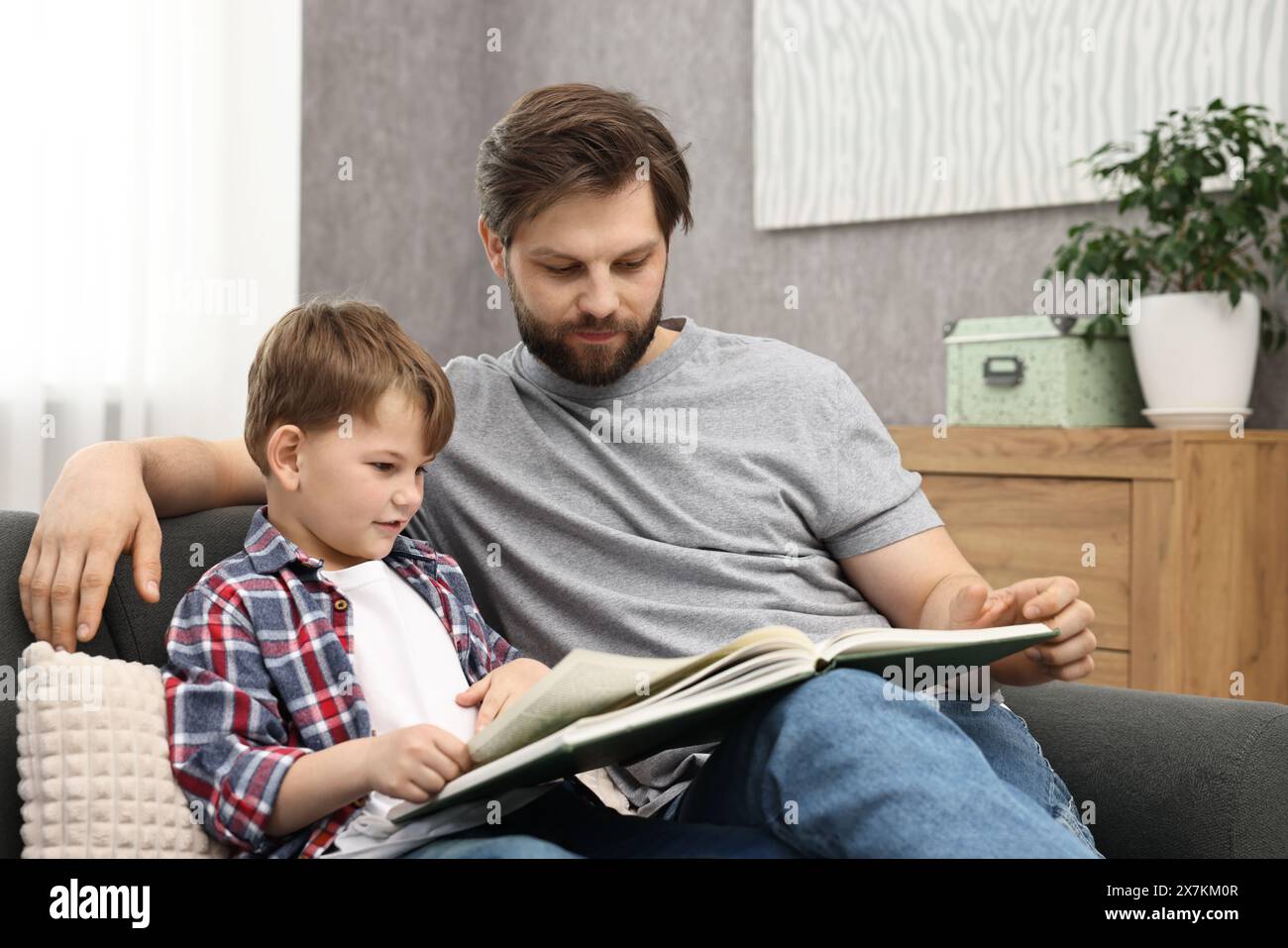 Dad and son reading book together on sofa at home Stock Photo - Alamy