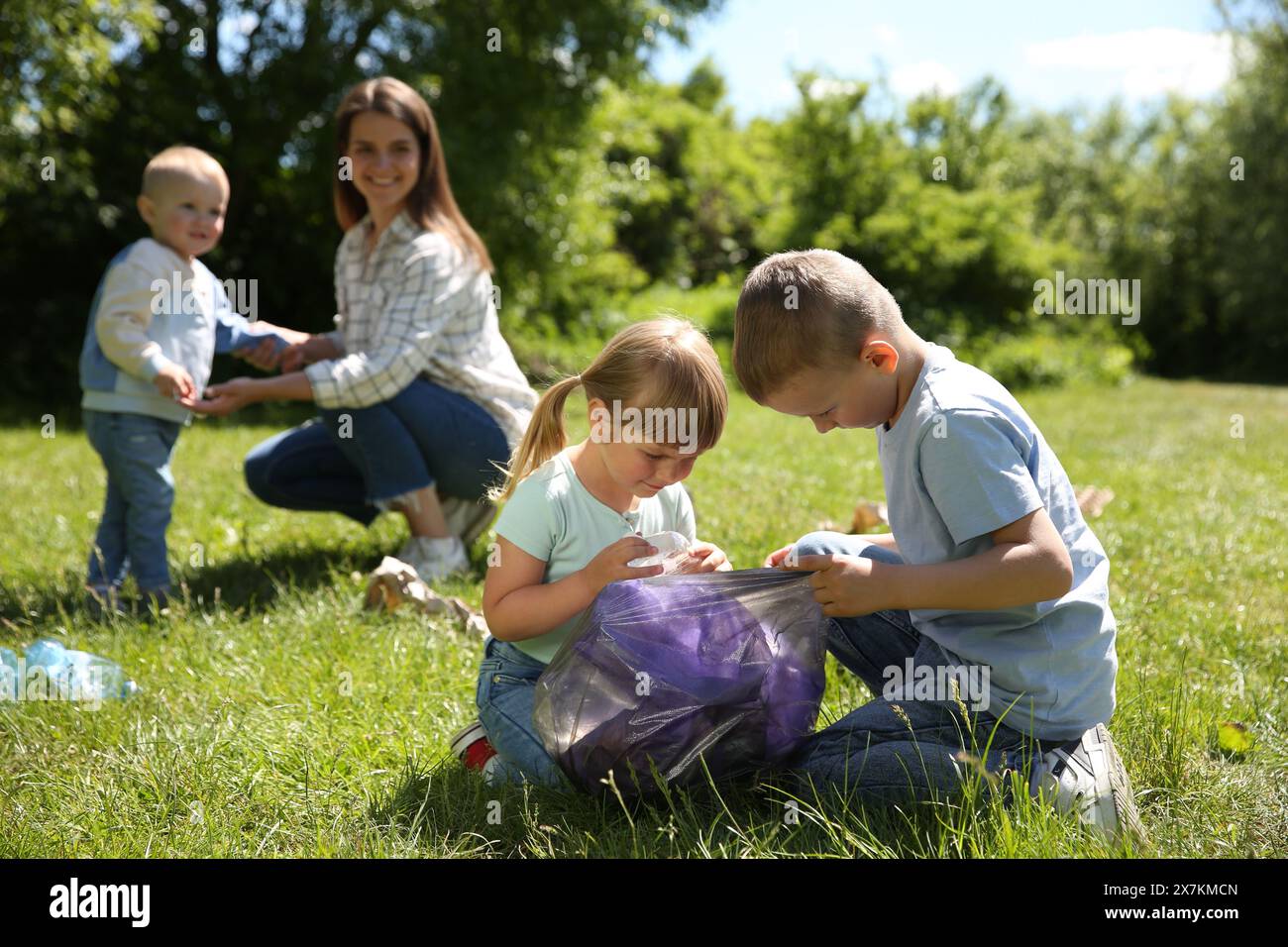 Mother and her children with plastic bags collecting garbage in park ...