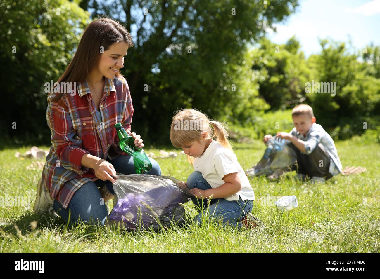 Mother and her children with plastic bags collecting garbage in park ...