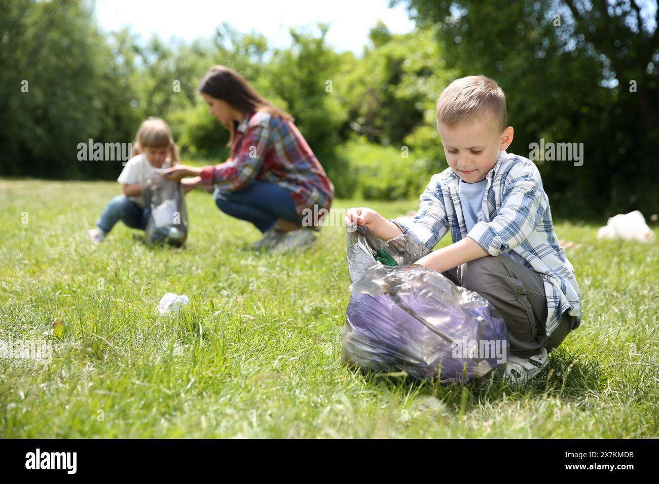 Mother and her children with plastic bags collecting garbage in park ...