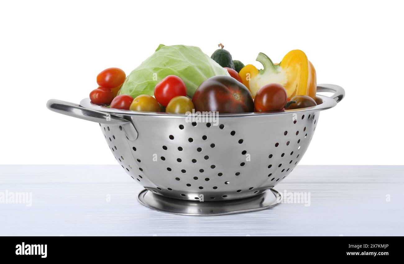Metal colander with different vegetables on table against white ...